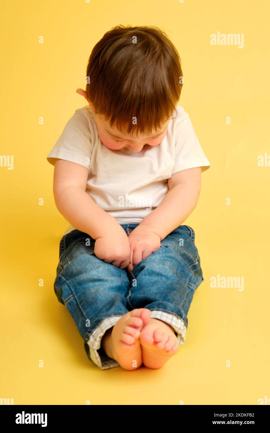Full length portrait of an embarrassed toddler baby on a studio yellow ...