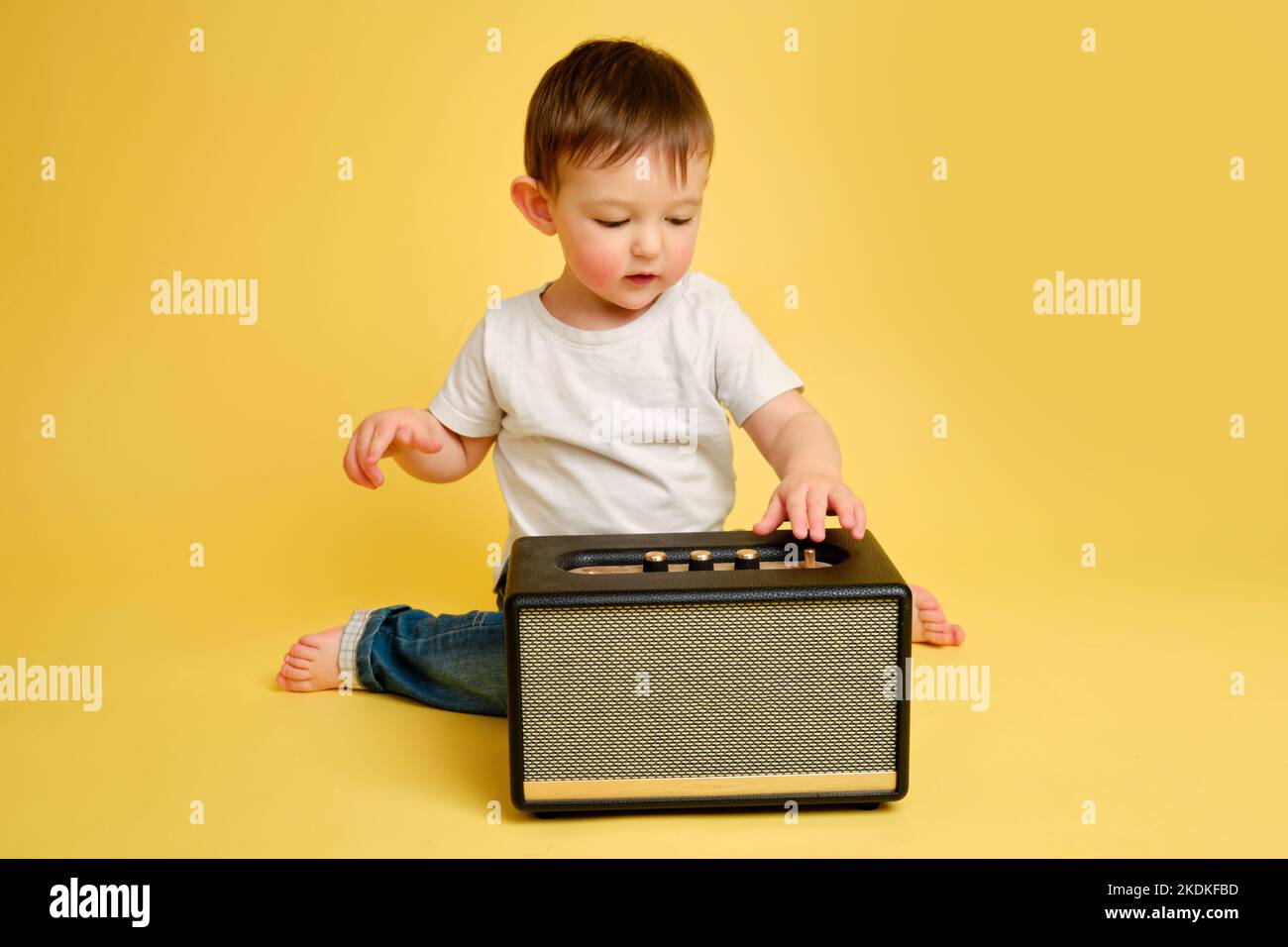 Toddler baby plays with a wireless music speaker on a studio yellow ...
