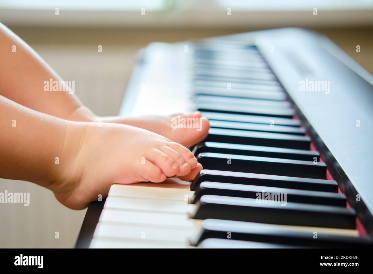 Toddler baby foot on electric piano keys, close-up. Child feet lie on ...
