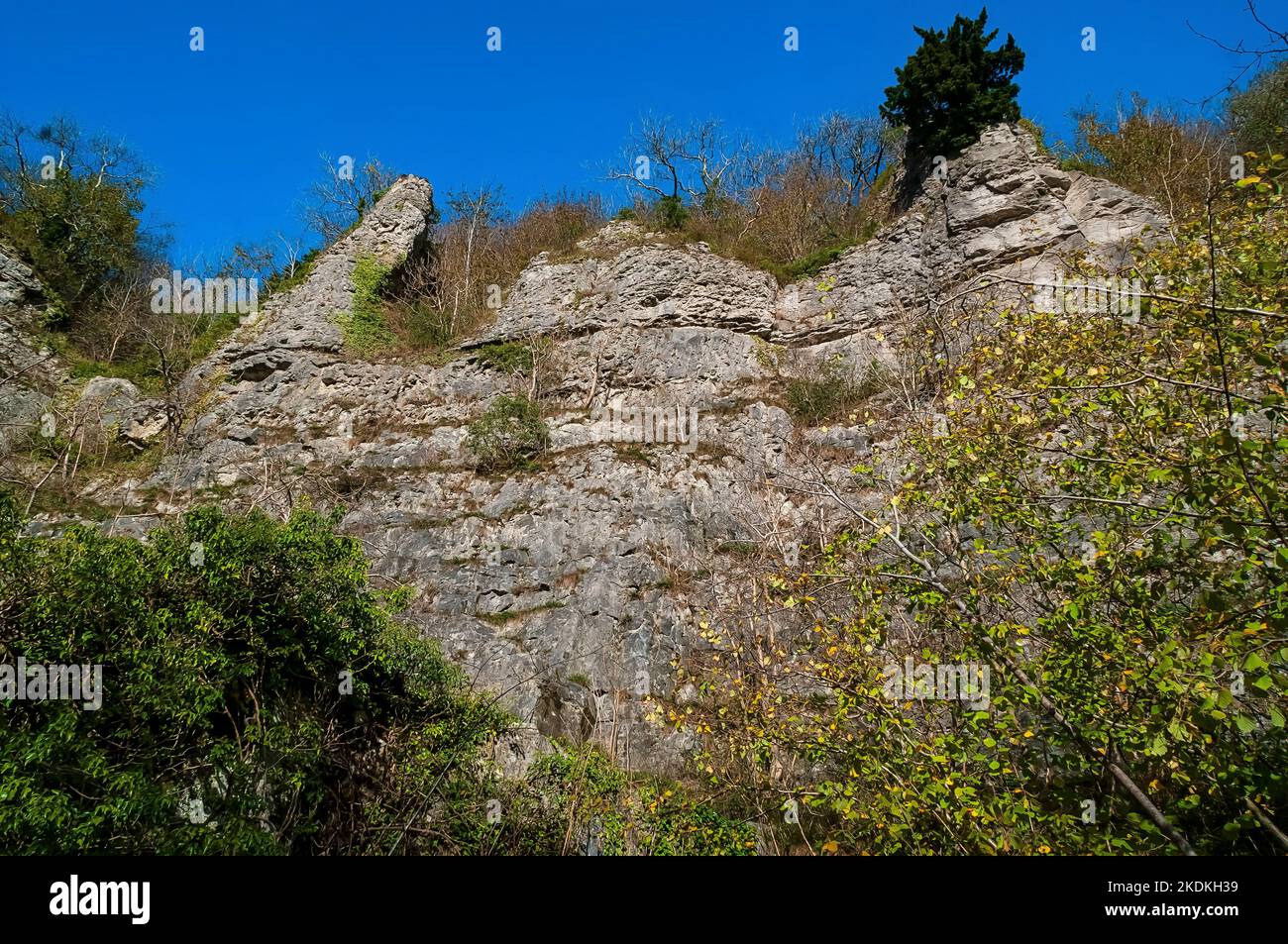 Tall limestone cliffs, partly quarried, with cave entrances and man ...