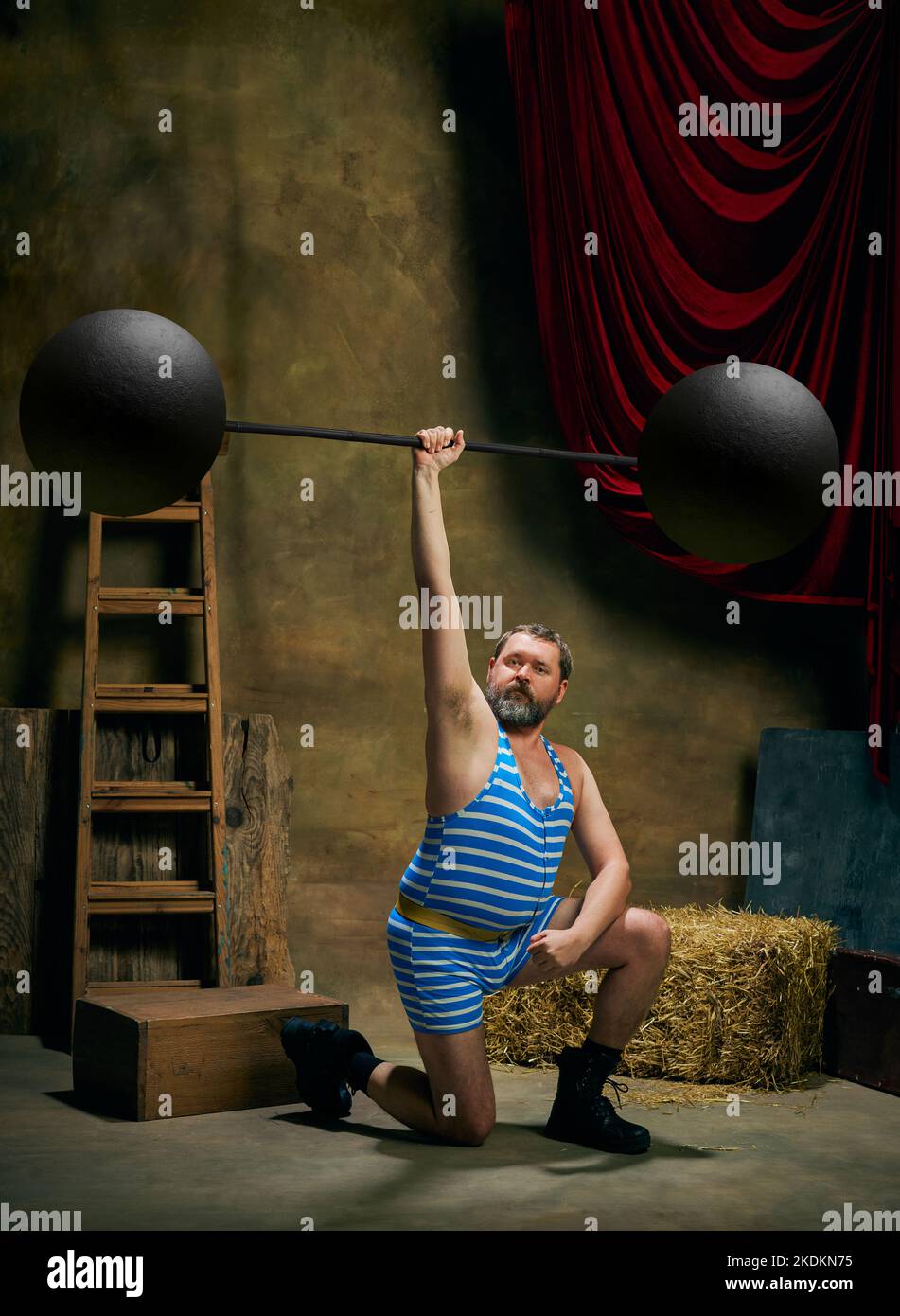 Overweight man, retro circus strongman wearing striped sports swimsuit ...