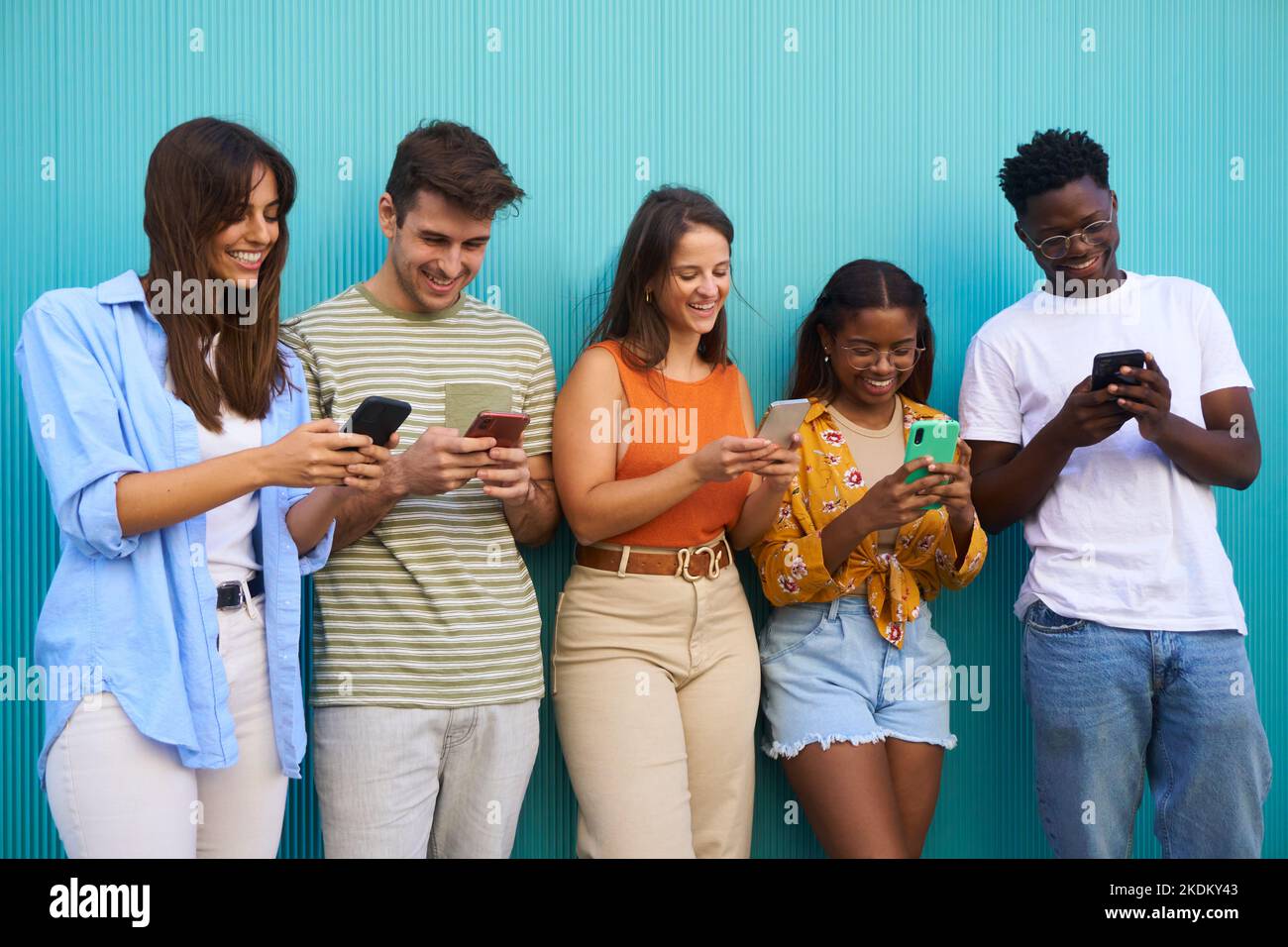 Group of mixed race young people using mobile phone outdoor. Students isolated in blue ...