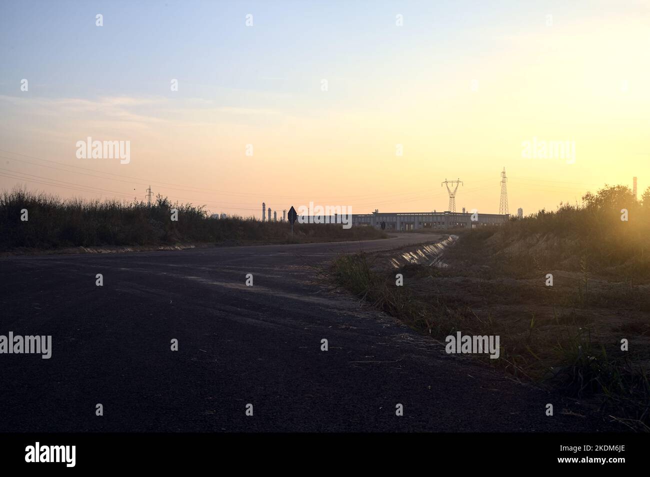 Entrance to an empty road that leads to abandoned warehouses at sunset ...