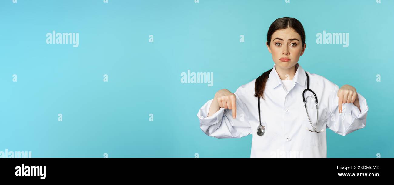 Sad and gloomy doctor, female medical worker pointing fingers down ...