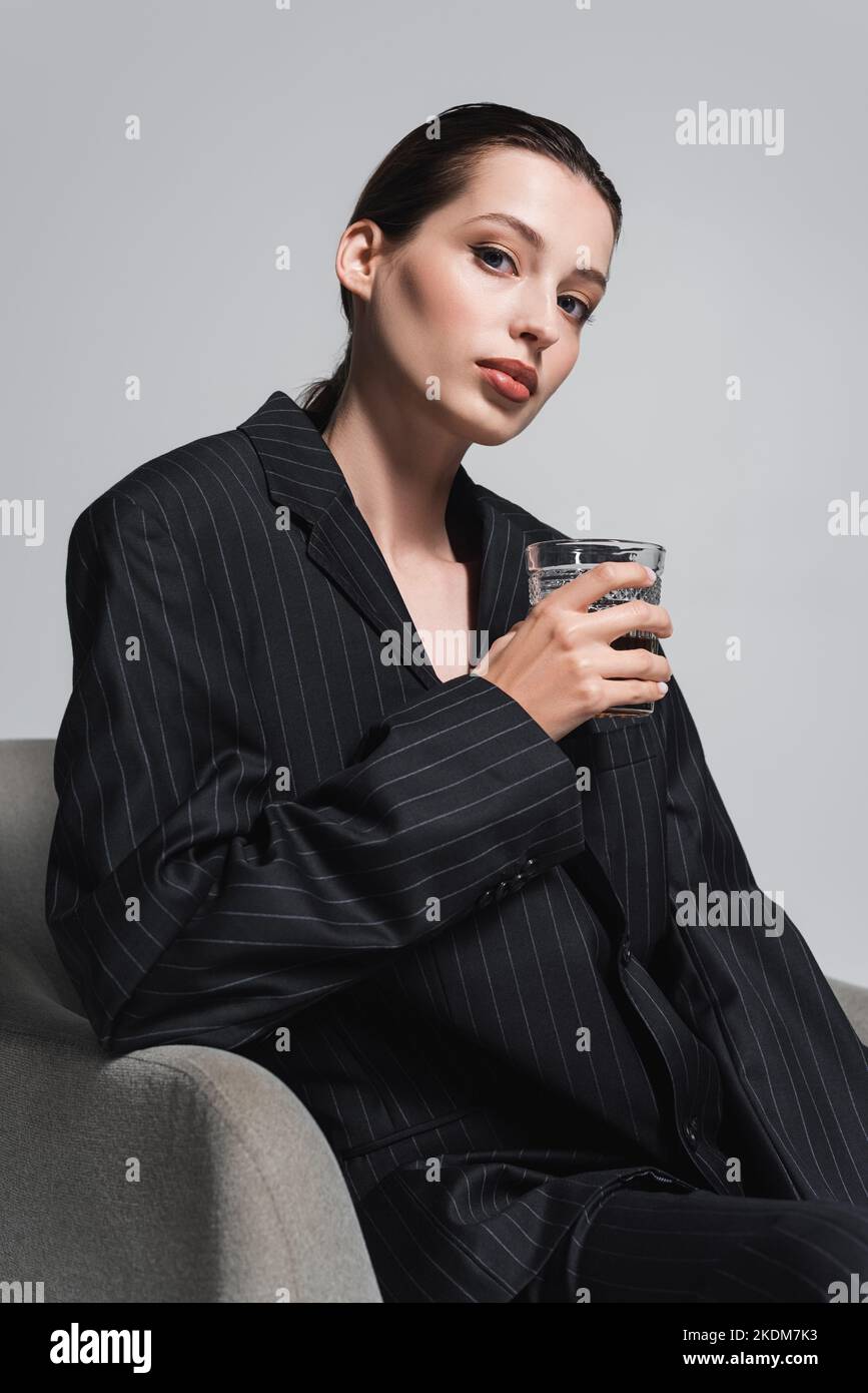Brunette model in stylish suit holding glass of bourbon while sitting ...