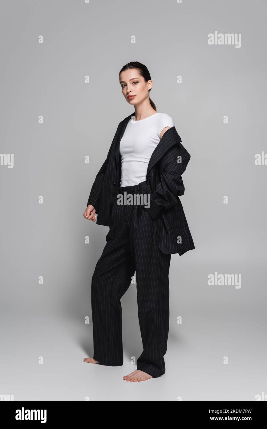 Full length of barefoot model in suit and t-shirt posing on grey ...