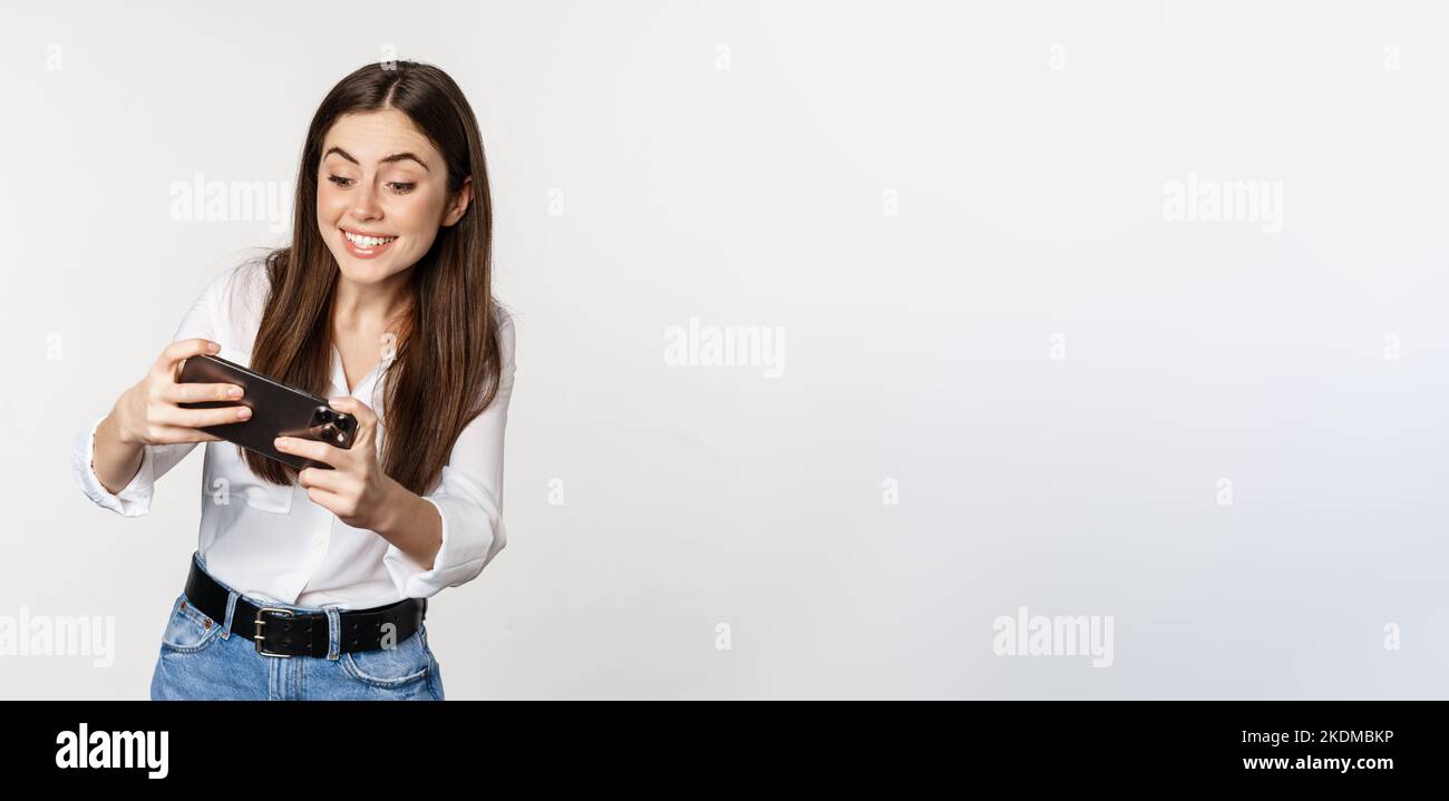 Happy brunette woman playing mobile video game, smiling and looking at ...