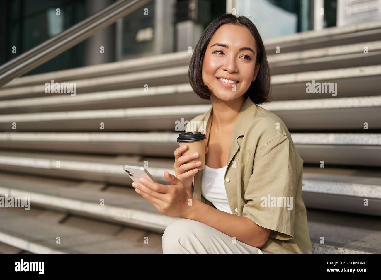 Happy urban girl drinks her takeaway coffee and scrolls feed on ...