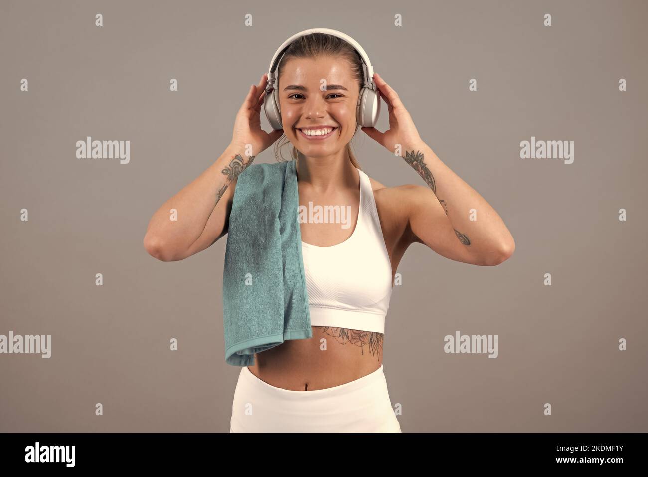 Young fitness woman runner with headphone and towel, isolated on gray ...