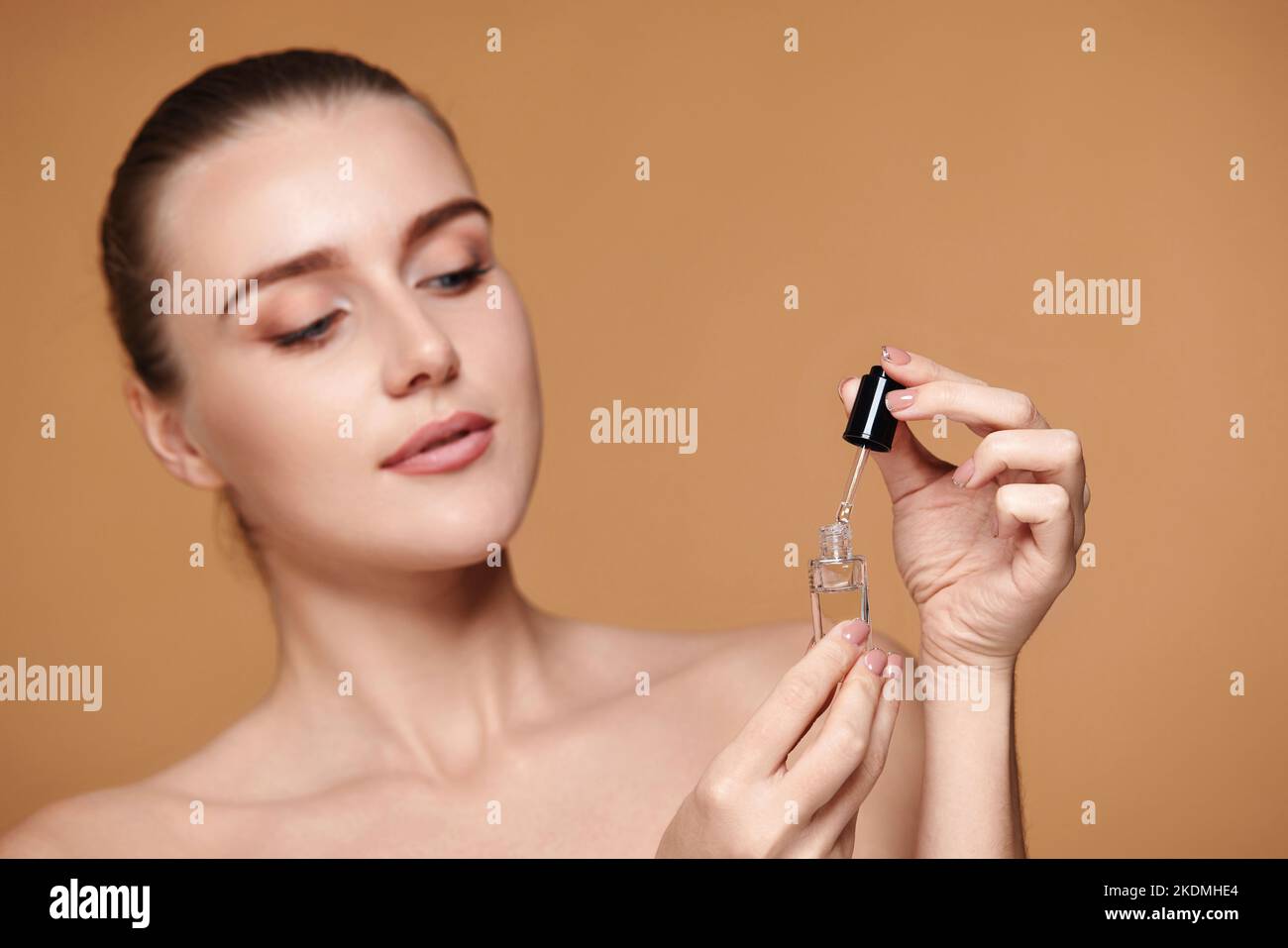 beautiful woman holding bottle with serum for skin care on beige ...