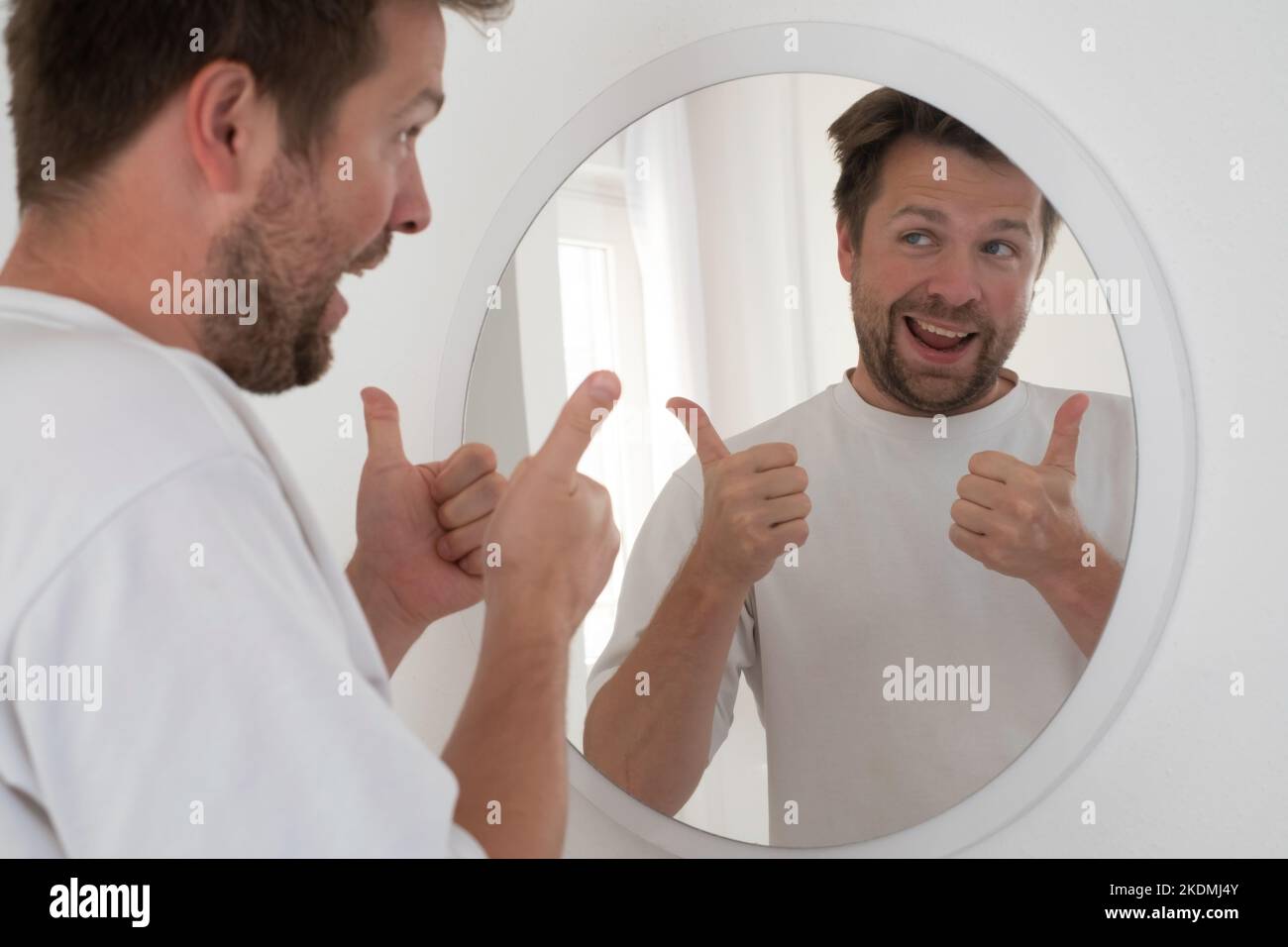 Man trying to encourage himself showing thumb up looking in mirror ...