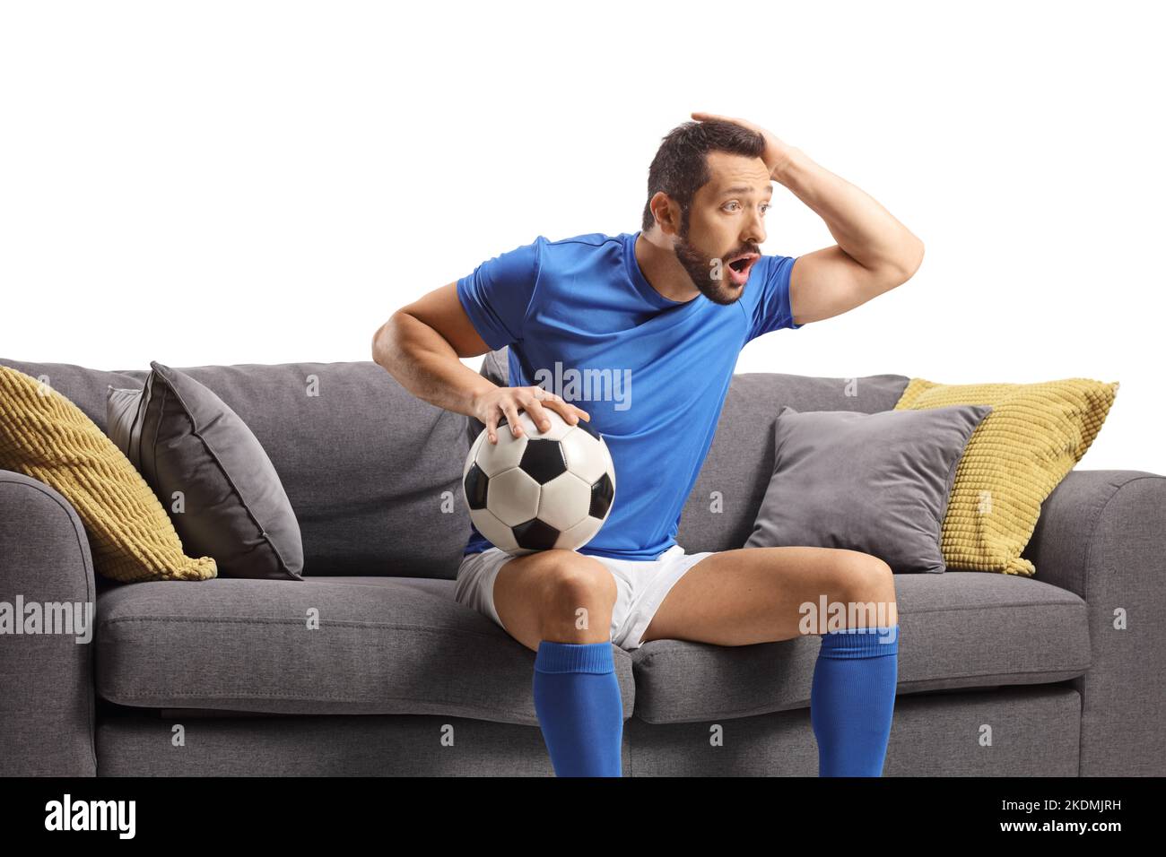 Surprised male athlete sitting on a sofa, holding a football and ...