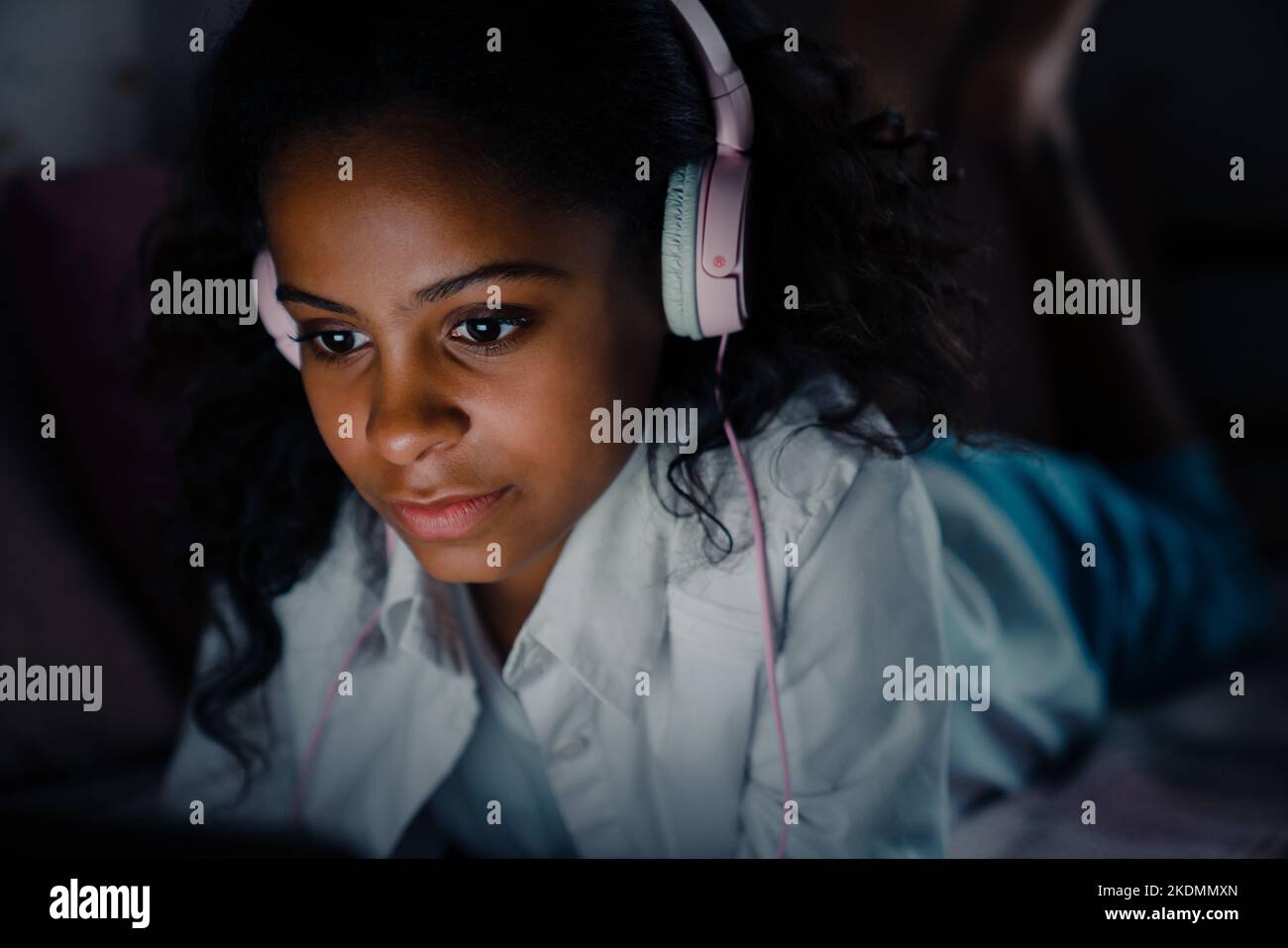 Young calm african girl in headphones liying in front of laptop looking ...