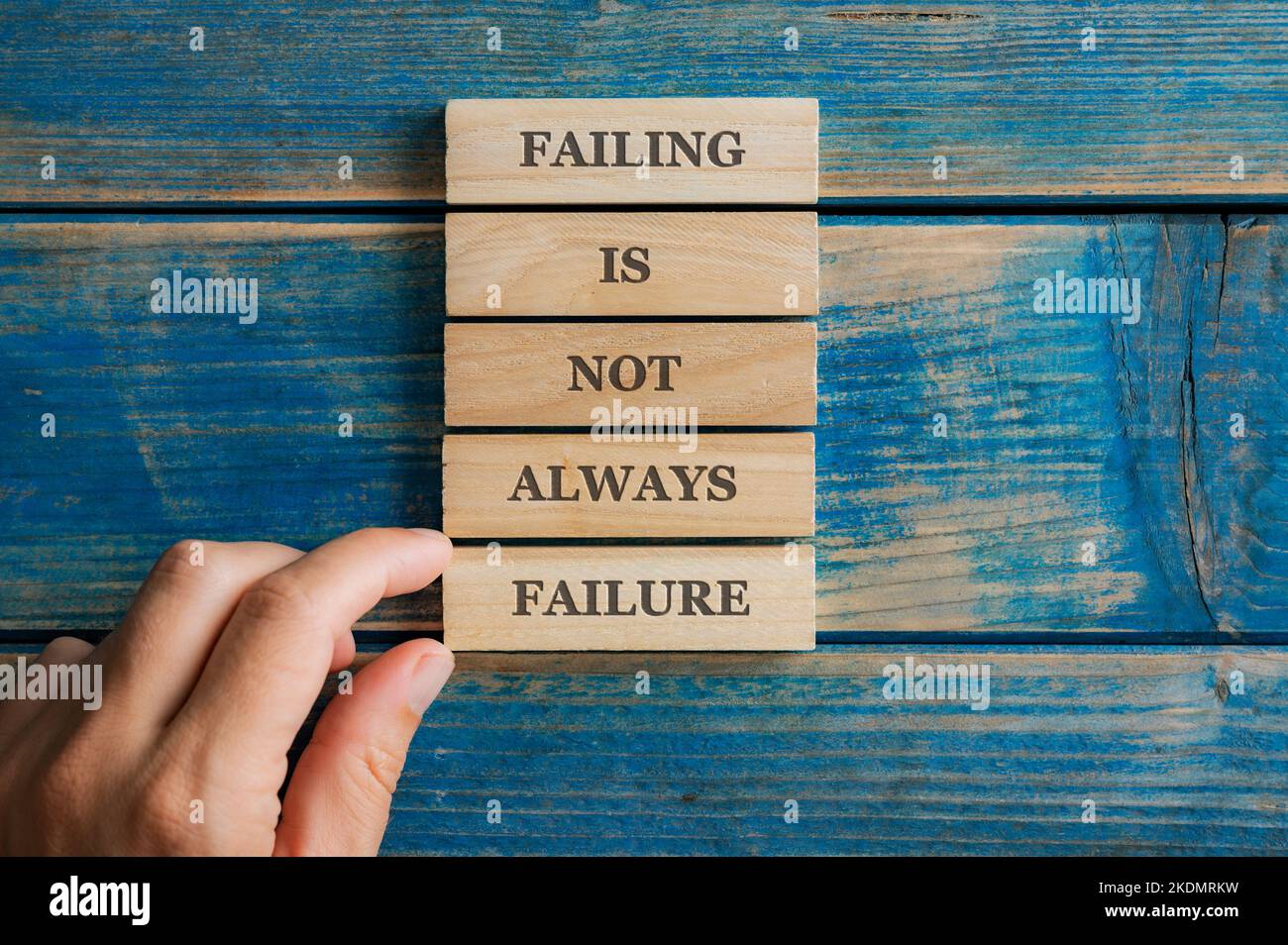 Male hand stacking five wooden pegs to spell the Failing is not a ...