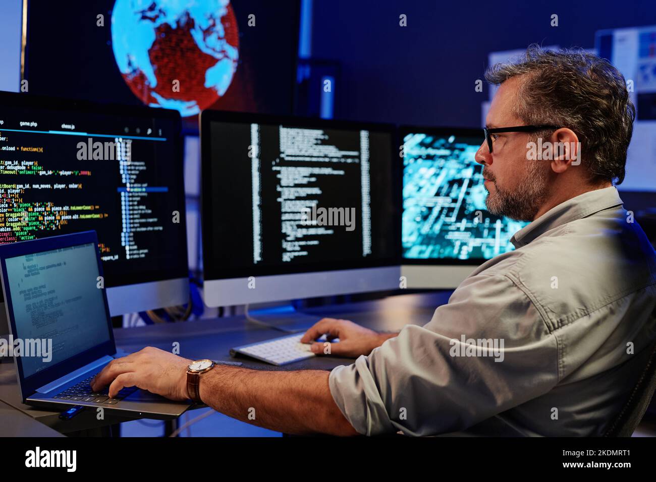 Side view of serious server engineer using laptop and computers while ...