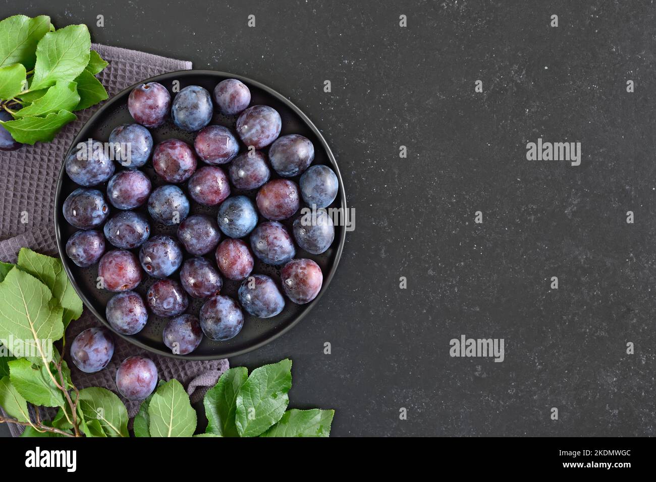 Fresh plums on plate over dark stone background with copy space. Top ...