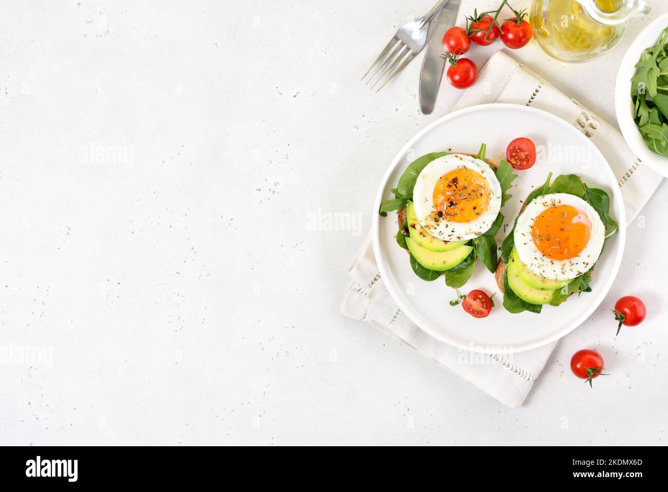 Bread with fried eggs, avocado and greens over light stone background ...