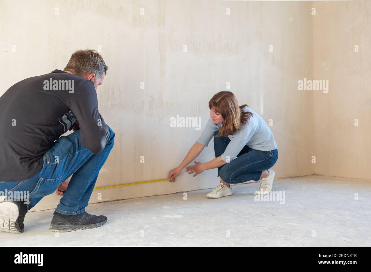 Young couple moving in new apartmen. People measure size of wall with ...