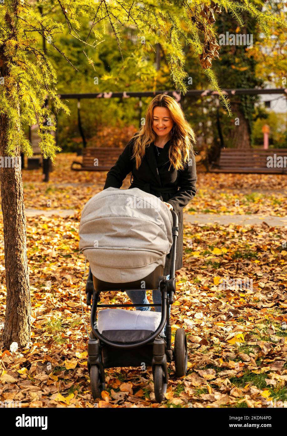 A happy mother smiling while looking at baby in a stroller during walk ...