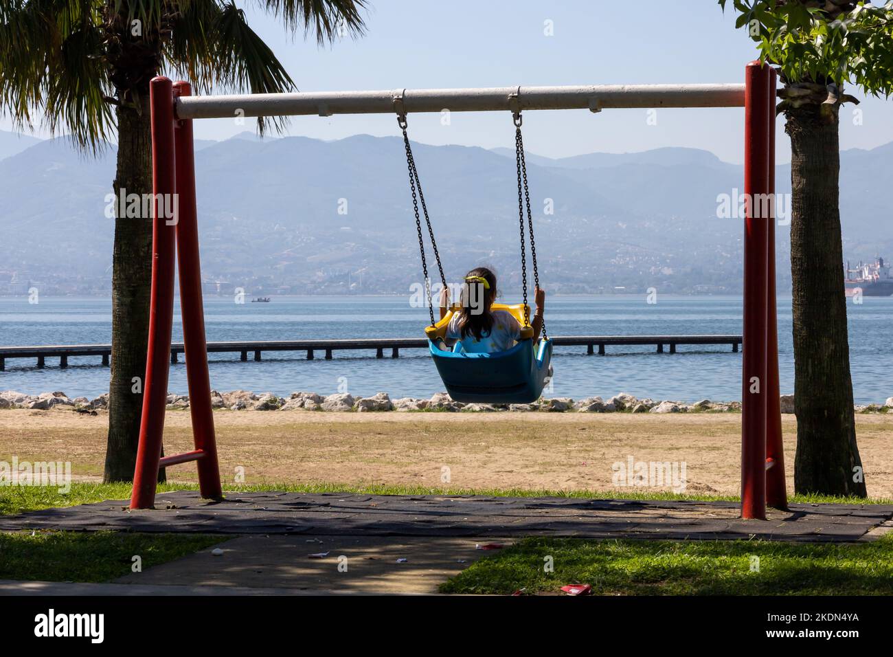 Kid ride on a swing against to sea. Little girl ride on a swing. Alone ...