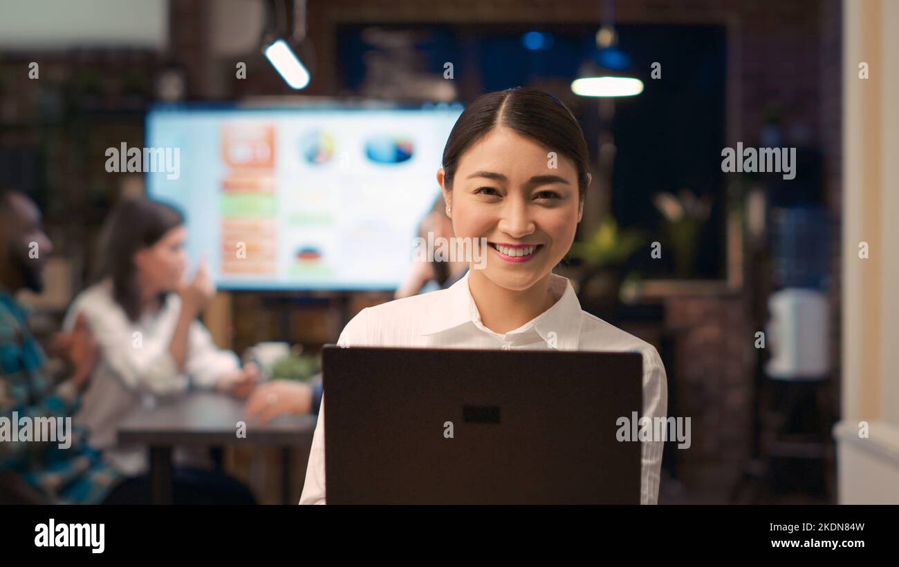 Asian employee working on laptop, looking at camera, smiling, slow ...