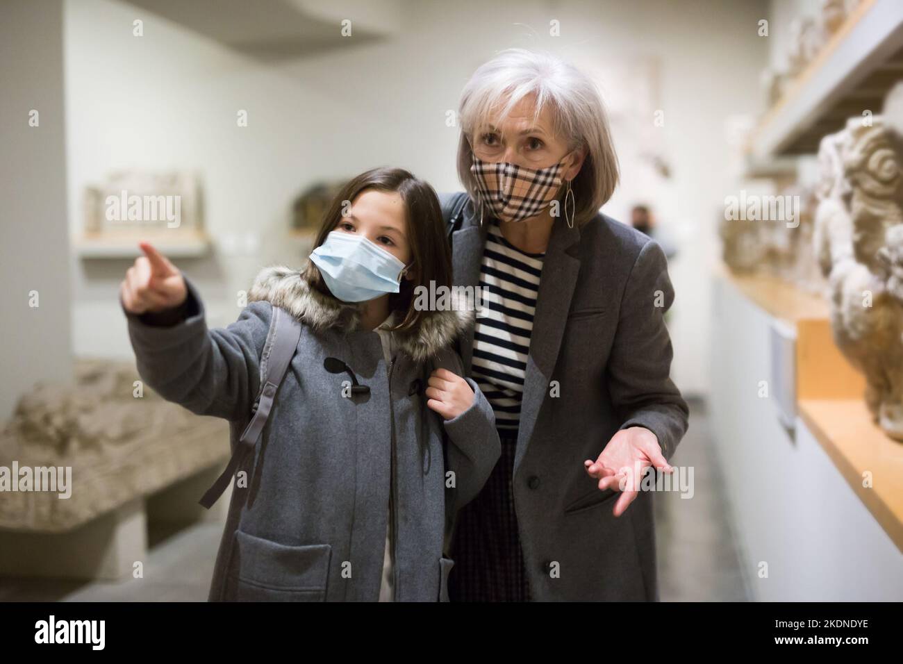 Elderly female tutor in protective mask showing tween girl ancient ...