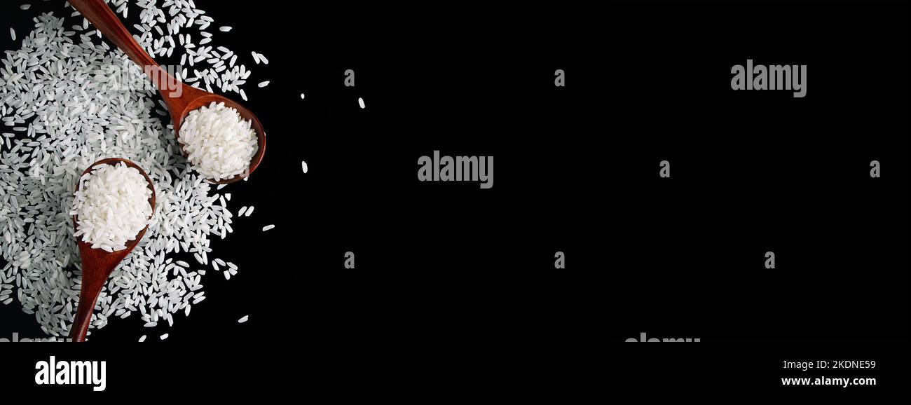 White long rice in wooden spoons on black background. Raw uncooked rice ...