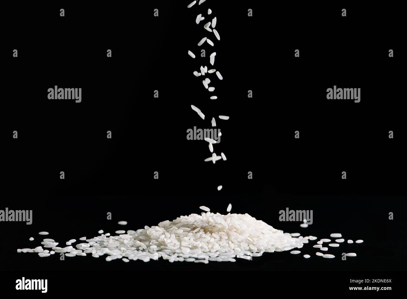 Raw white rice is falling on table. Pile of uncooked long rice on black ...