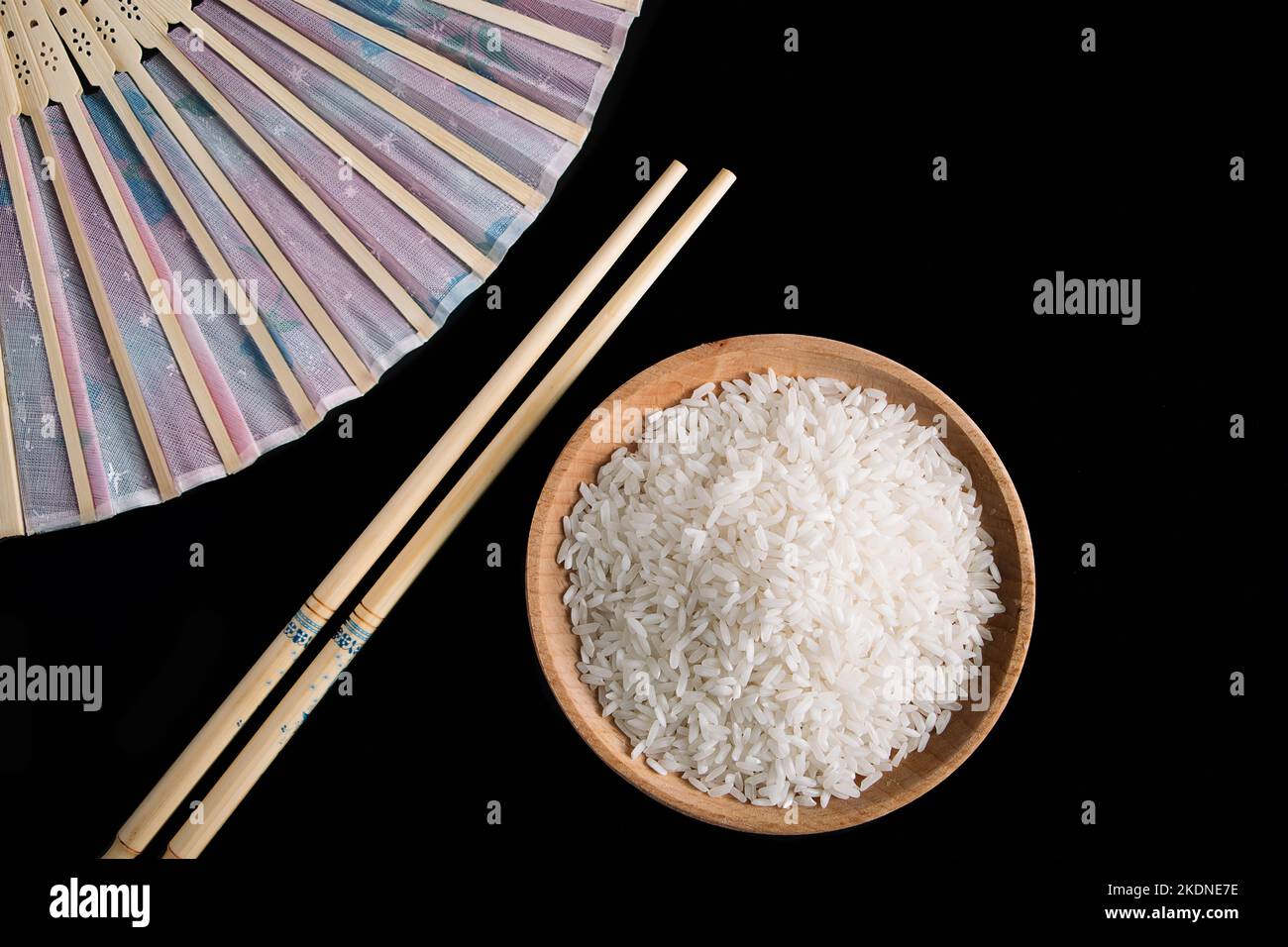 Raw white rice, hand fan and chopsticks on black background. Long ...
