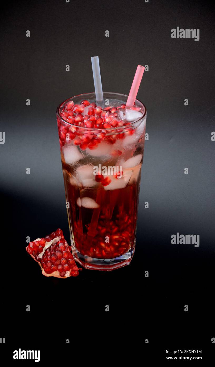 Tall glass of pomegranate juice with ice and straws on a black ...