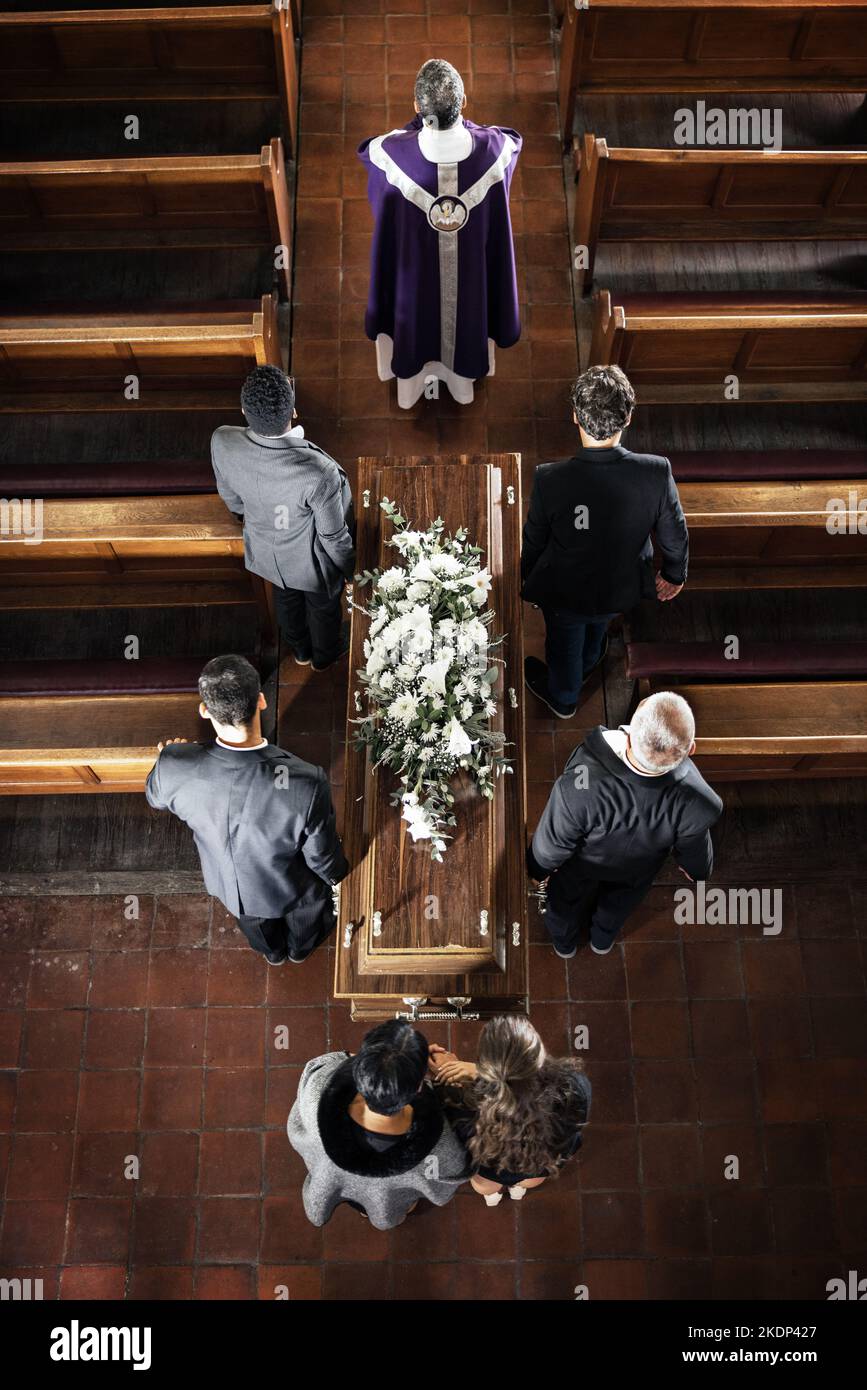 Funeral, church and sad people carrying coffin with a priest ...