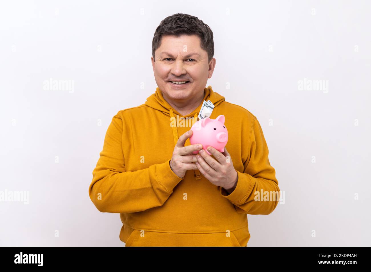 Portrait of smiling middle aged man holding piggy bank with banknote in ...