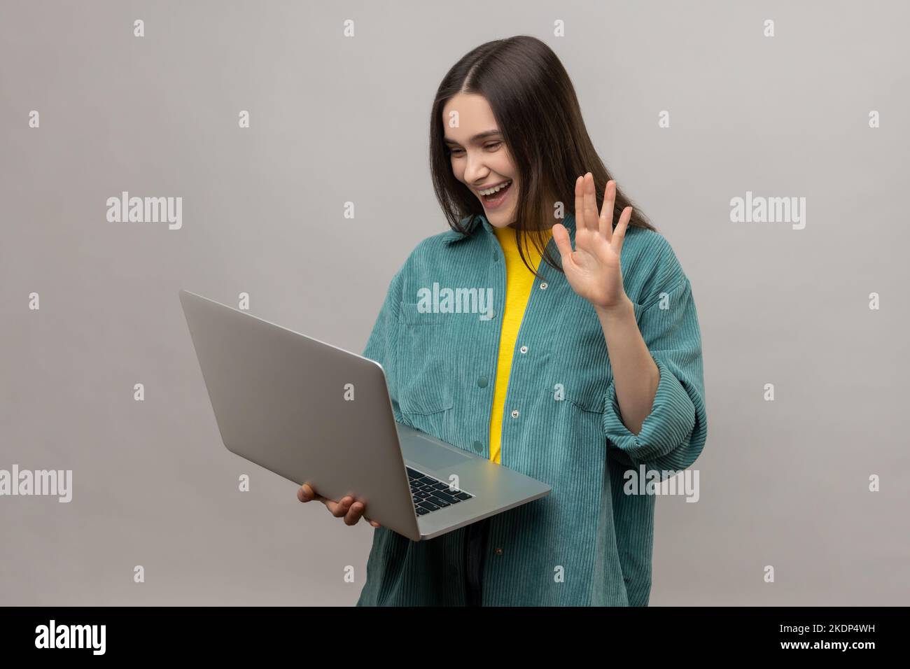 Beautiful woman with dark hair waving hand, gesturing hello to laptop ...