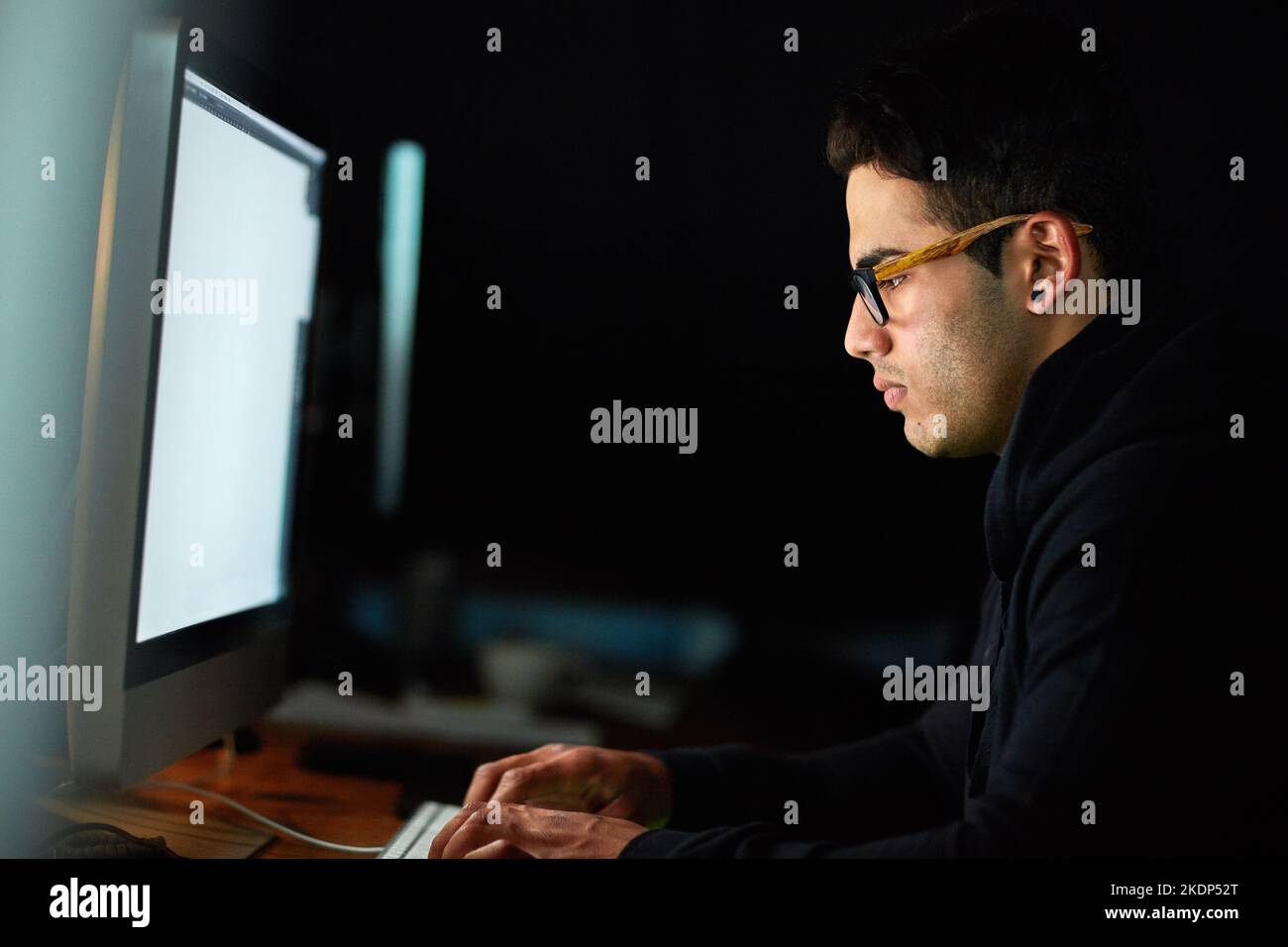 Working by the light of his monitor. a young hacker cracking a computer ...