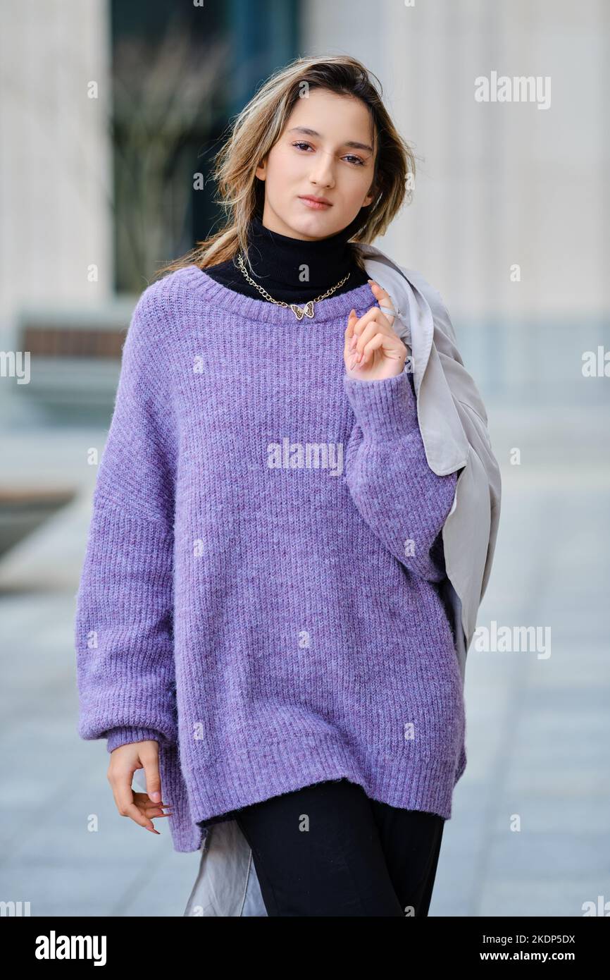 Young woman walking on the street and holds raincoat over her shoulder ...