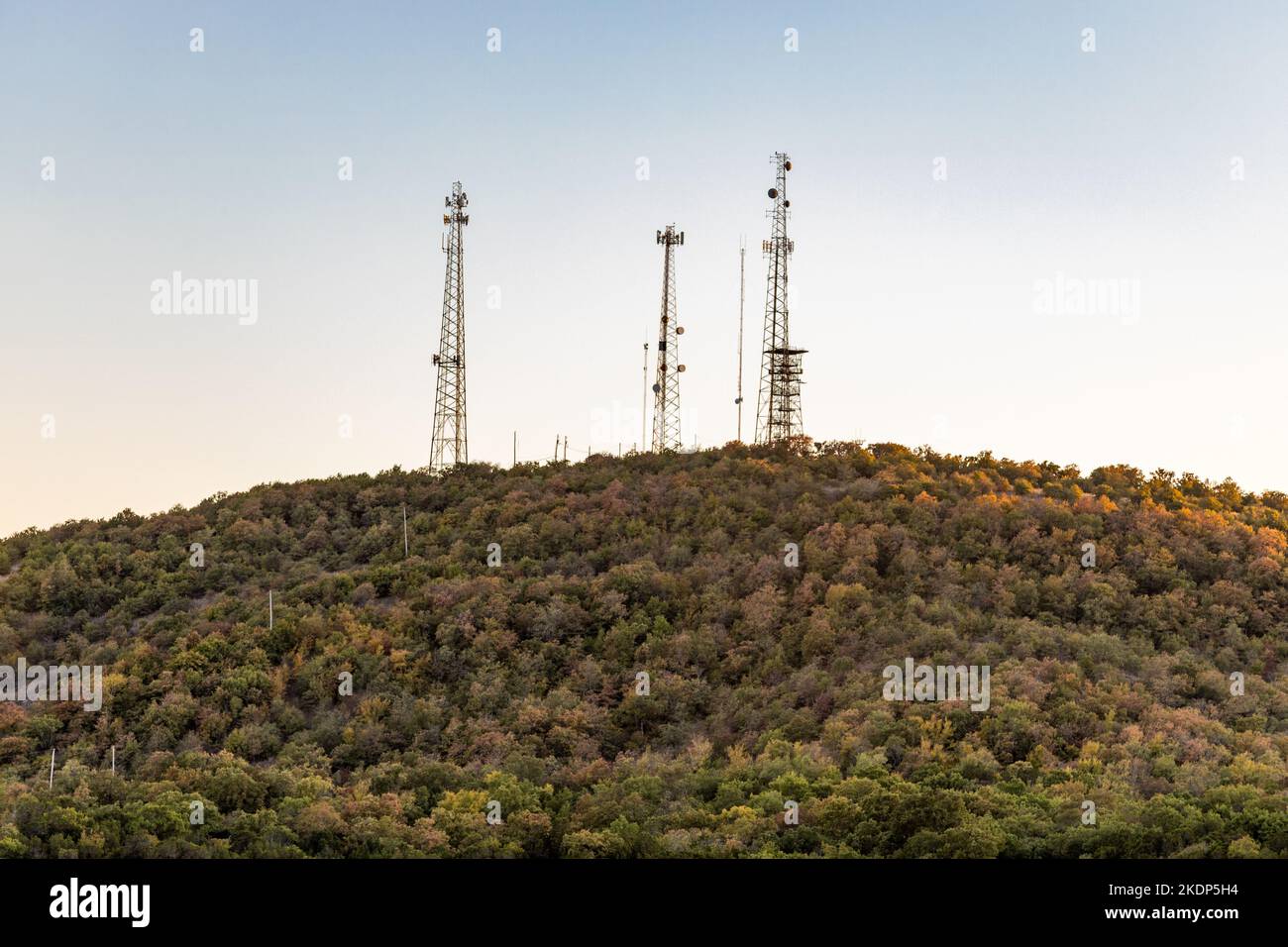 Communication antennas on the light blue sky and hills with forest ...