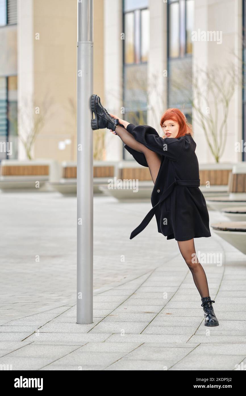 Flexible young woman shows splits by putting her foot on a lamppost ...