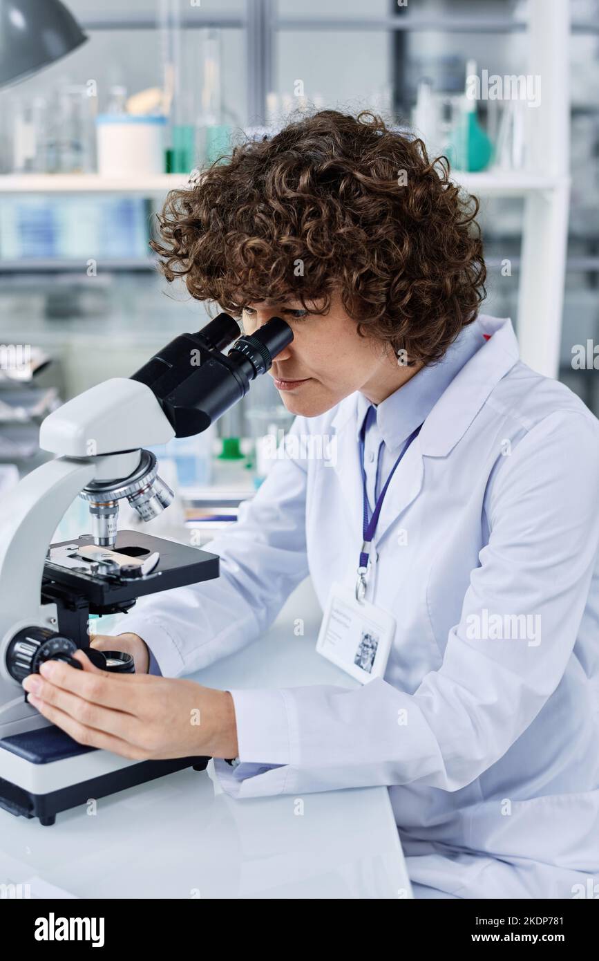 Young chemist or virologist in labcoat looking in microscope while ...