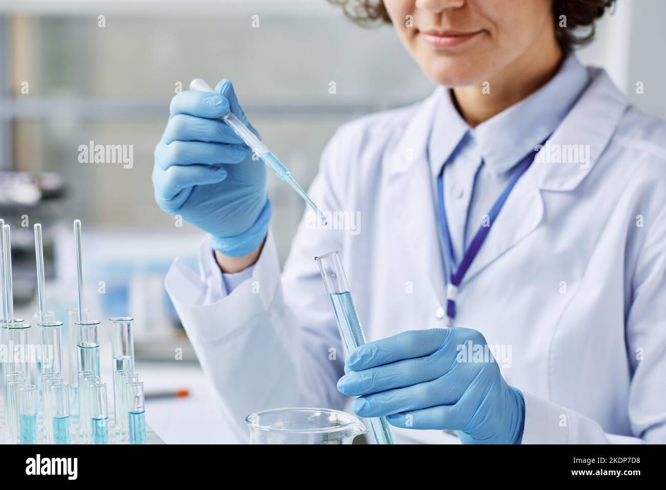 Young laboratory worker in gloves and labcoat dropping liquid substance ...