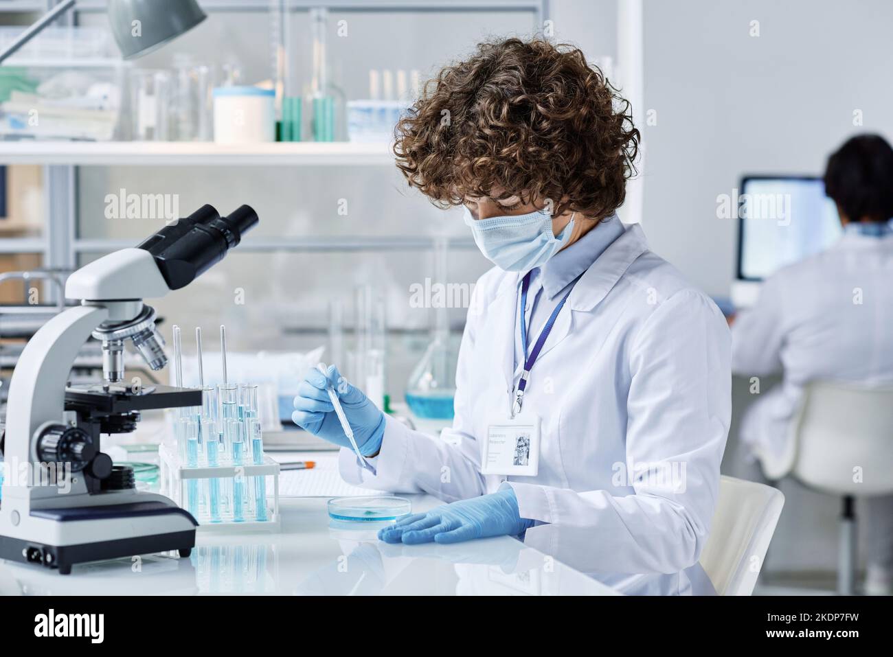 Young biochemist in protective workwear bending over desk while mixing ...