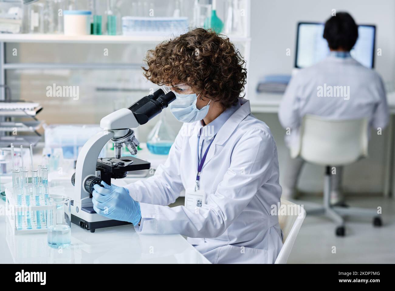Young woman in labcoat, protective mask and gloves looking in ...