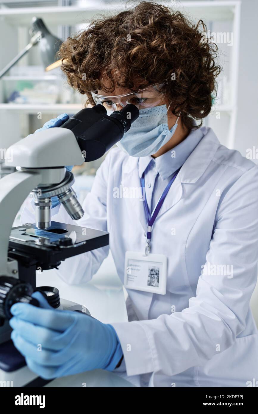 Young serious female virologist in protective mask and gloves studying ...