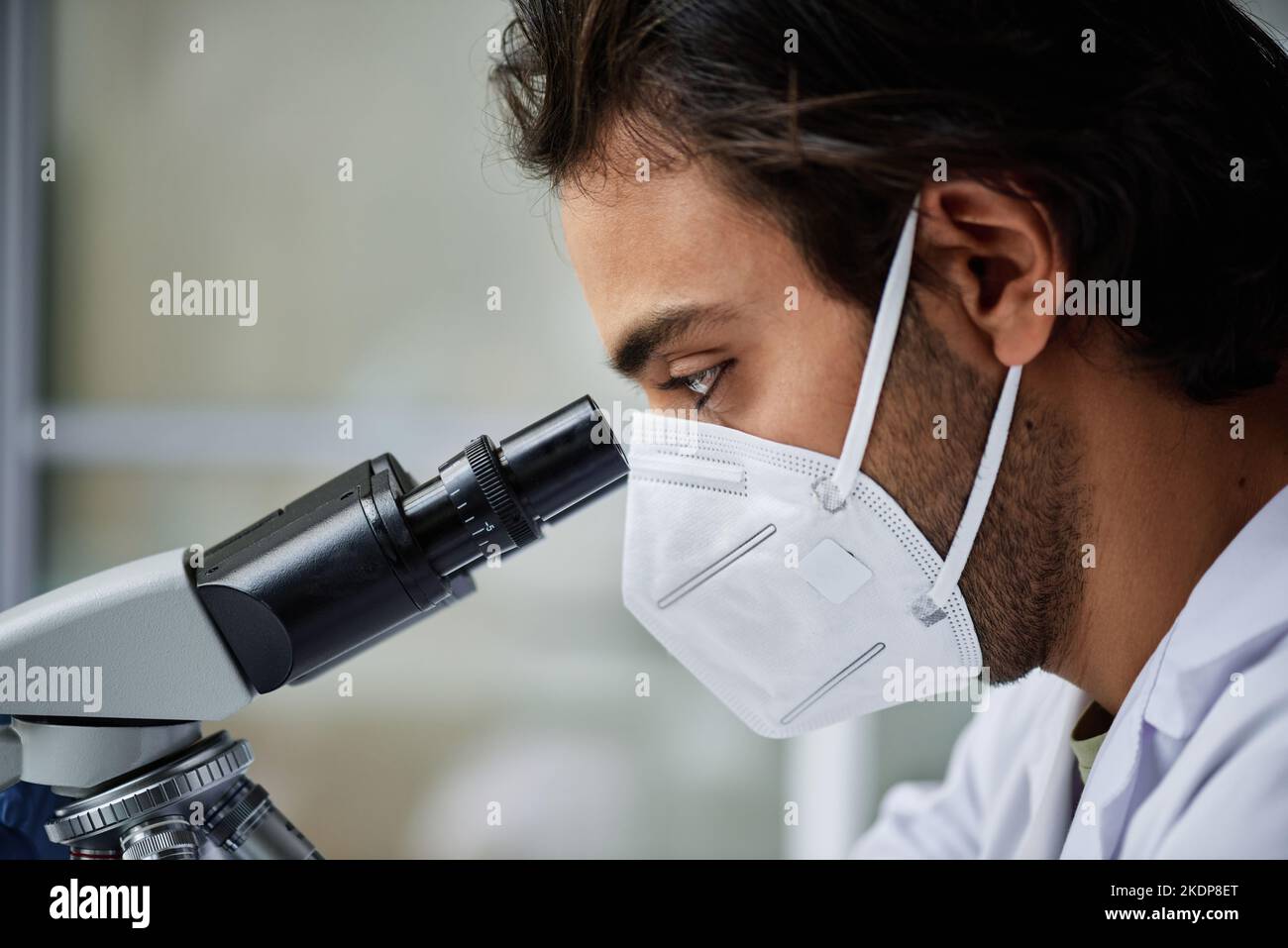 Close-up of young man in respirator looking in microscope in laboratory ...