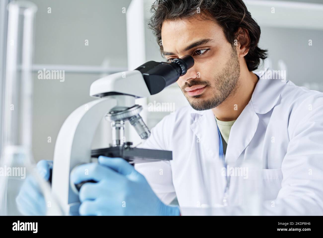 Young serious virologist in labcoat studying new bacteria or virus and ...