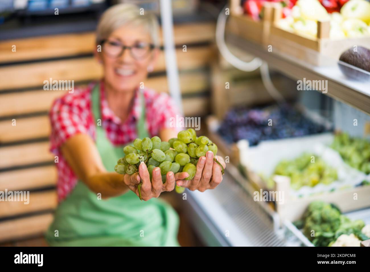 Woman works in fruits and vegetables shop. She is examining grapes ...