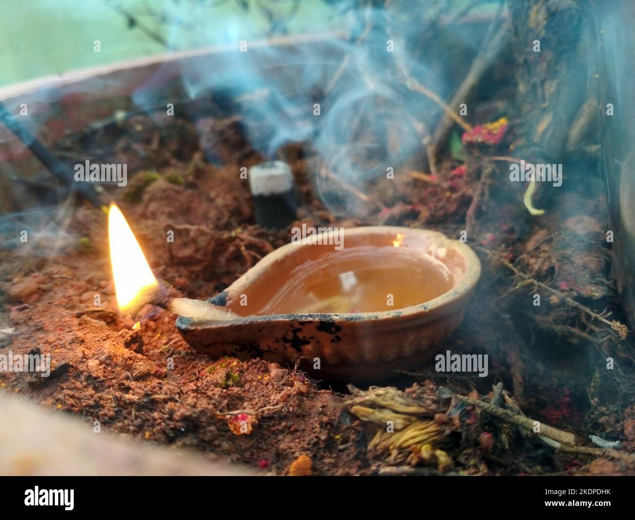 Clay diya with a small flame sits on soil, surrounded by incense smoke ...