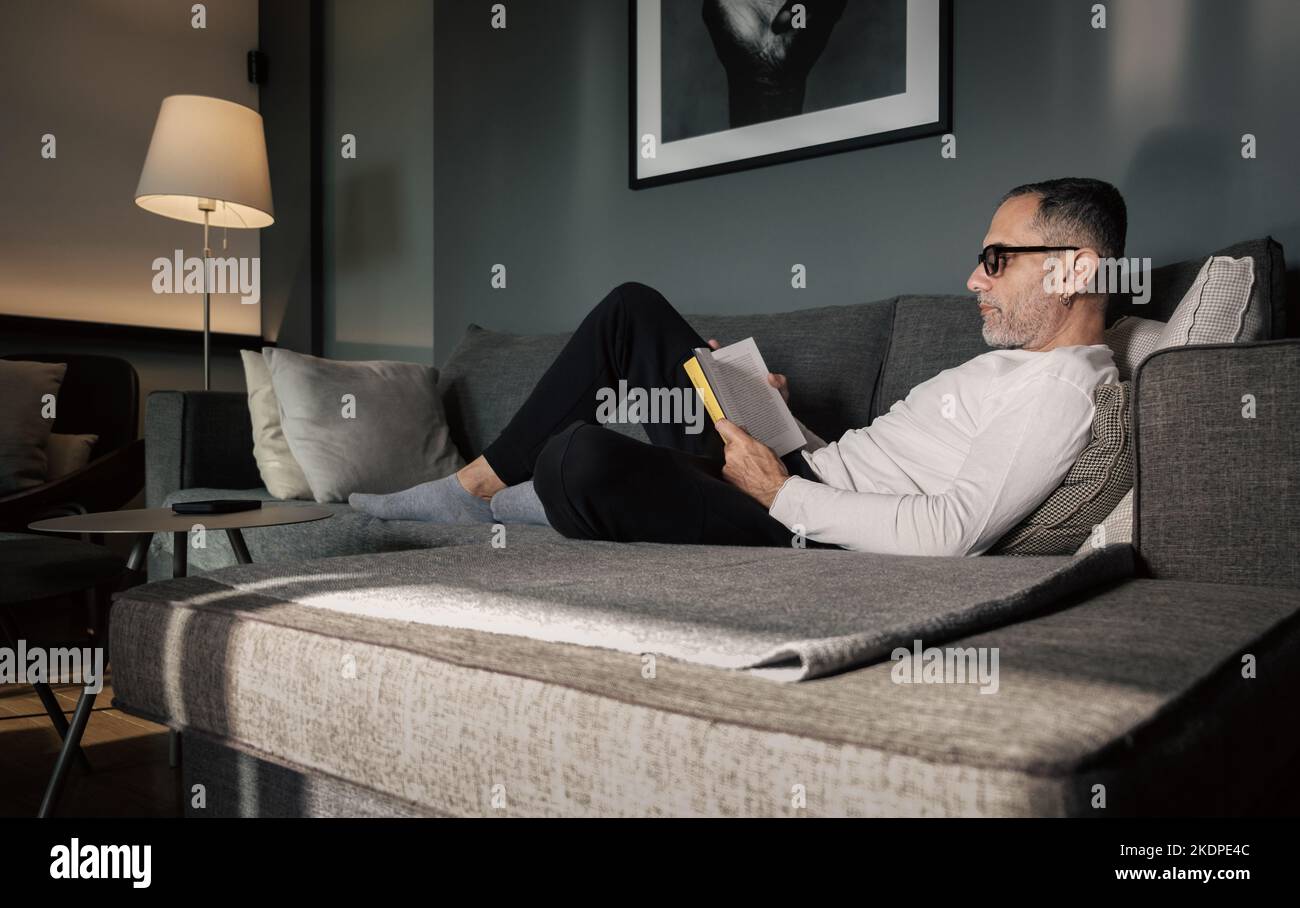 Man reading book on couch Stock Photo - Alamy