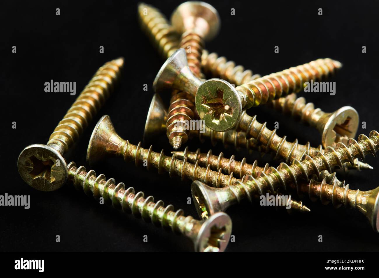 Pile of screws or self-tapping screws with a yellow coating on a black ...
