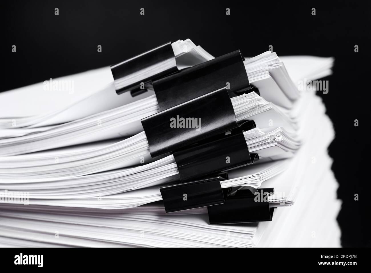 A stack of office papers, some of which are fastened with black binders ...