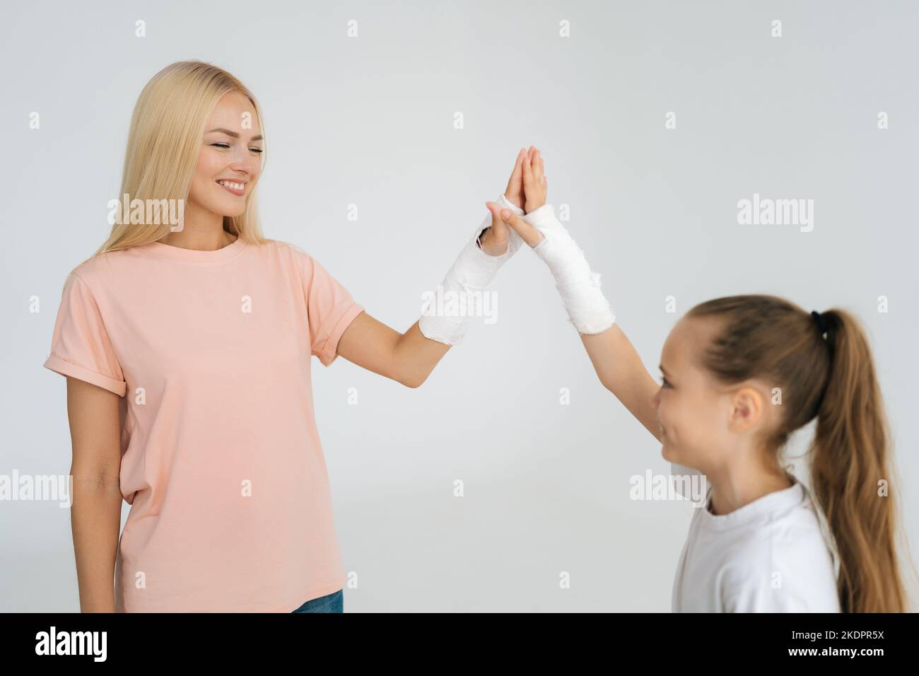Studio shot of cheerful injured blonde young woman and little kid girl ...
